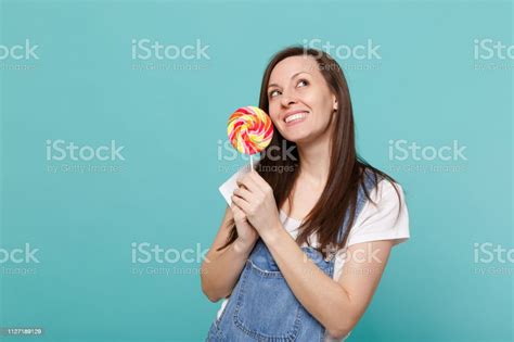 데님 옷 들고 화려한 찾고 Dreamful 웃는 젊은 여자의 초상화 스튜디오에서 블루 터키석 벽 배경에 고립 된 롤리팝 라운드 사람들의 라이프 스타일 개념입니다 복사 공간을