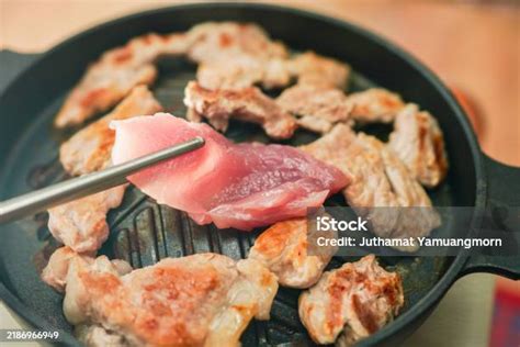 스테인레스 젓가락을 사용한 손으로 생 돼지 고기 또는 돼지 고기 바베큐를 냄비에 구워 아시안 스타일로 먹을 수 있습니다 건강한