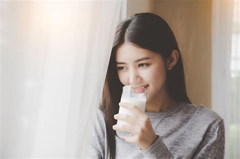행복 하 고 웃는 얼굴로 집에서 아침에 신선한 우유를 마시는 아름 다운 젊은 아시아 여자 우유 한 잔을 들고 매력적인 소녀