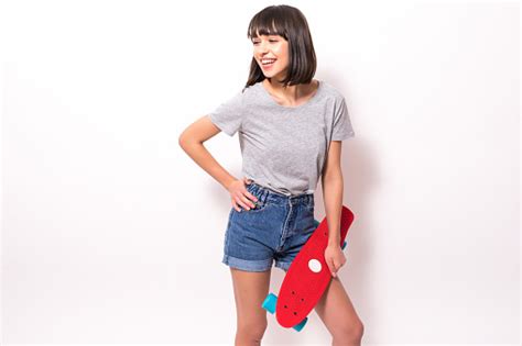 서 있고 흰색 배경 위에 고립 된 카메라를 보고 있는 동안 스케이트 보드와 함께 포즈 선글라스에 예쁜 젊은 여자의 전체 길이 초상화 명랑한에 대한 스톡 사진 및 기타 이미지