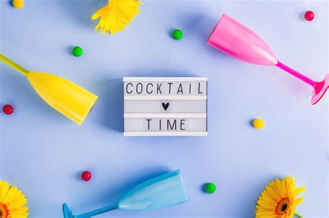 칵테일 타임 비문 밝은 플라스틱 칵테일 안경 멀티 컬러 캔디 드롭 보라색 파란색 배경에 노란색 거베라 꽃이있는 라이트 박스의