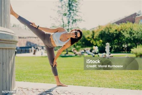 갈색 머리 여자의 전체 길이 샷은 다리를 뻗어 좋은 유연성을 보여줍니다 활동적인 선글라스 포즈 외부 리드 활동적인 라이프 스타일을 입고 분할 않습니다 사람들은 스포츠와