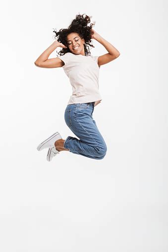 청바지와 티셔츠점프를 입고 흰색 배경에 고립된 완벽한 미소로 기뻐하는 아프로 헤어 스타일을 가진 사랑스러운 미국 여성의 전체