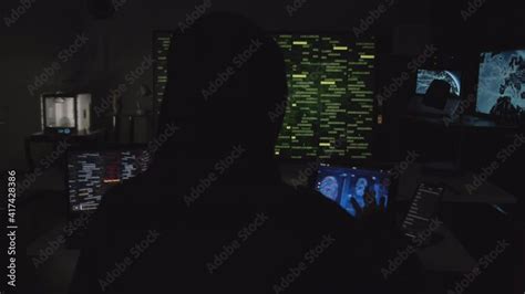 hooded hacker working on computer dark room with devices playing