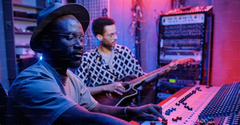 스타일리시한 성숙한 아프리카계 미국인 프로듀서가 믹서에서 소리를 조절하는 동안 젊은 음악가가 기타를 연주하는 장면 사진