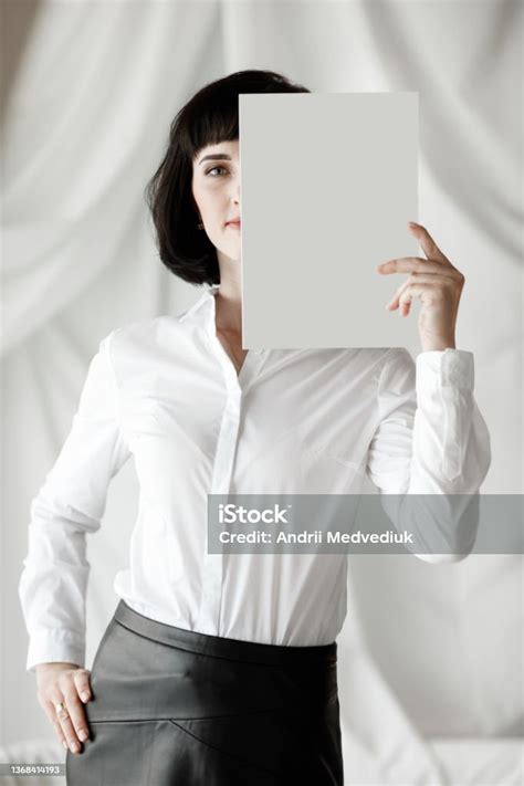 잡지를 들고 어두운 짧은 머리를 가진 아름다운 젊은 여자 모의와 함께 책 스튜디오에 서있는 흰색 셔츠와 검은 가죽 스커트에 소녀 30 34세에 대한 스톡 사진 및 기타