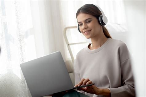 헤드폰을 착용하고 노트북 컴퓨터를 사용하면서 음악을 듣고 거실에서 즐겁게 노래하고 즐기는 행복한 젊은 여성 엔터테인먼트가있는 행복 여성 라이프 스타일 개념 가정 생활에 대한