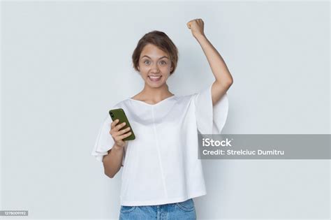 젊은 백인 여자 몸짓 에 이 승리 기호 들고 전화 와 미소 에 A 흰색 스튜디오 벽 골인에 대한 스톡 사진 및 기타 이미지 골인 놀라움 도박 Istock