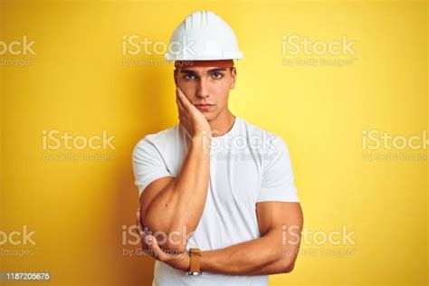 노란색 고립 된 배경 생각에 건설 헬멧을 착용 하는 젊은 잘 생긴 남자 피곤 하 고 교차 된 팔우울증 문제로 지루 해 보이는