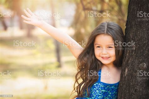 신발 없이 파란 드레스를 입고 공원에서 놀고 있는 아름다운 행복한 소녀는 아이들의 날을 즐기는 가족들과 함께 행복하게 비명을 지르며 나무에 앉아 있다 4 5세에 대한 스톡