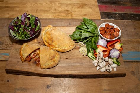 맛있는 칼존 피자 컷은 요리를 만드는 데 사용되는 재료로 둘러싸인 나무 테이블에 맛있는 피자 토핑을 공개합니다 고기에 대한 스톡