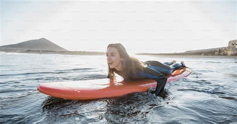 잠수복을 입은 젊은 여자는 서핑 보드에서 물의 흐름을 잡고 일몰 동안 물결 모양의 바다에서 서핑을 합니다 수상 스포츠와 활동적인 라이프 스타일 개념 사진