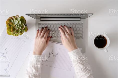 커피 한 잔과 함께 사무실 테이블에 앉아 종이에 인쇄 된 그래픽과 차트와 노트북에서 작업하는 동안 여성 프리랜서 작업 및 노트북의 키보드에 입력 플랫 레이 거래자에 대한