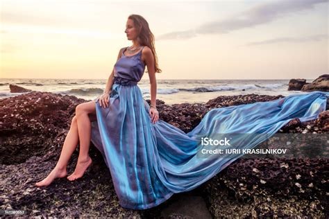 화려한 스타일의 갈색 머리 젊은 여성 블루 카멜레온 드레스 긴 기차 바다 근처 바위에 서 바위에 모래 열대아름다운 인어 외로운 우울한 대기 자유와 프리랜서 드레스에 대한