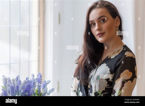 Attractive Dark Haired Girl Posing Next To Purple Flowers In Windows Stock Photo Alamy