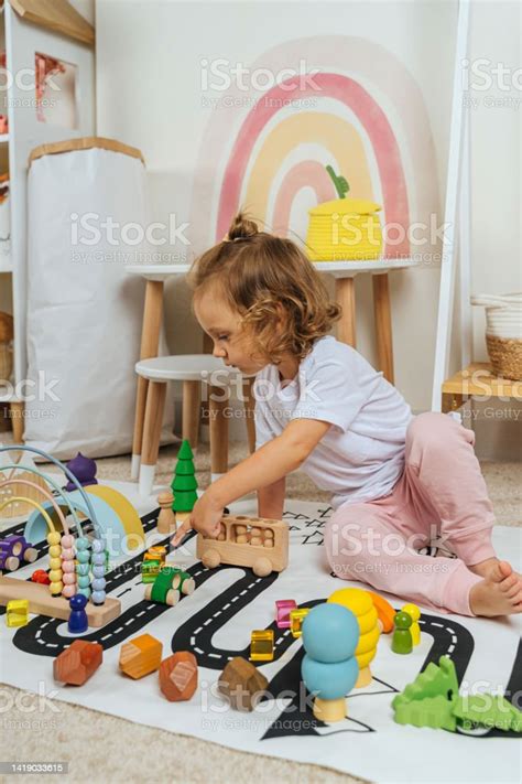 바닥에 앉아있는 어린 소녀는 놀이방에있는 도로 그림이있는 양탄자에 장난감 자동차와 나무 블록을 가지고 놀고 있습니다 현대 보육원에서 아기와 유아를위한 교육 게임 2 3 살에
