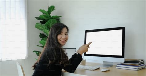 직장에서 컴퓨터 앞에 앉아 있는 동안 휴대폰을 들고 카메라에 미소를 짓는 행복한 사업가의 측면 모습 사진 Unsplash의