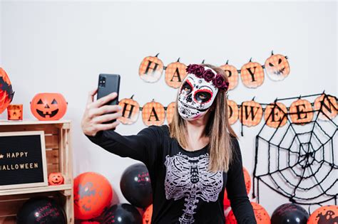 할로윈 축하 기간 동안 멕시코 얼굴 마스크를 착용 하는 여자 휴대 전화로 셀카를 찍는 스켈레톤 의상과 빨간 장미 디아뎀을 머리에 쓰고 있는 여성 할로윈 파티 컨셉 10월에