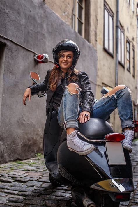 Beautiful Girl Wearing A Leather Jacket And Ripped Jeans Sitting On A Black Classic Scooter On