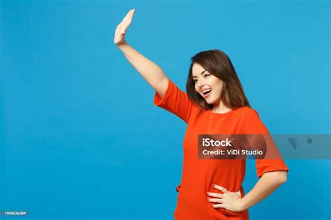 빨간 오렌지 드레스를 입고 아름 다운 젊은 여 자가 파란색 배경 스튜디오 초상화 위에 고립 된 통지로 손을 흔들며 인사말 사람들의 라이프 스타일 패션 컨셉 복사 공간을 모의