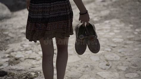 Dolly View Of A A Woman Walking Barefoot Along A Stone Path With Shoes In Hand Stock Footage