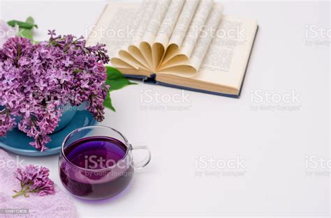 향기로운 보라색 클리토리아 차 한 잔과 파란색 컵에 라일락 꽃다발 흰색 배경에 열린 책 선택적 초점 낭만적 인 개념 수평 배경