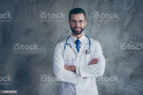 긍정적 인 쾌활한 수염 의사 성공적인 의료 노동자 개념 크로스 손의 초상화 는 회색 색상 배경 위에 고립 된 흰색 유니폼을 입고 질병을 치료 할 준비가 갈색 머리에 대한