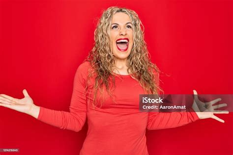 고립 된 배경에 서 빨간색 캐주얼 티셔츠를 입고 젊은 아름다운 금발 의 여자 미친 미친 소리와 공격적인 표정과 팔을 제기 고함 좌절 개념입니다 T 셔츠에 대한 스톡 사진 및