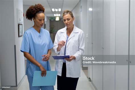 의료 차트 문서를보고 병원 복도에 서 있는 두 명의 다양한 여성 의사 2명에 대한 스톡 사진 및 기타 이미지 2명 간호사