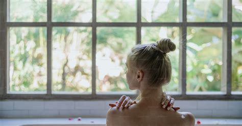 유기농 스킨 케어 개념 벌거벗은 어깨를 만지고 허브와 꽃이 있는 욕조에 누워 있고 욕실에서 쉬고 있는 젊은 성인 소녀의