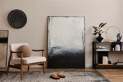 모형 포스터 프레임 부클 안락의자 검은색 랙 말린 꽃병 격자 무늬 책 패턴 러그 베이지 벽 개인 액세서리가 있는 아늑한 거실