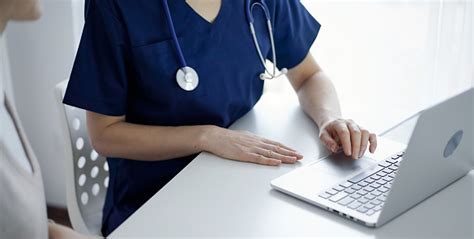 의사와 환자가 진료소 사무실의 책상에 앉아 있다 초점은 노트북 컴퓨터를 사용하여 알 수없는 여성 의사의 손에 있습니다 의학 개념