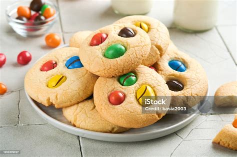 다채로운 초콜릿 사탕과 우유로 만든 수제 쿠키 밝은 회색 배경에 우유 병이있는 접시에 여러 가지 색의 사탕이있는 쇼트 브레드 쿠키가 쌓여 있습니다 이유식 개념 공간을