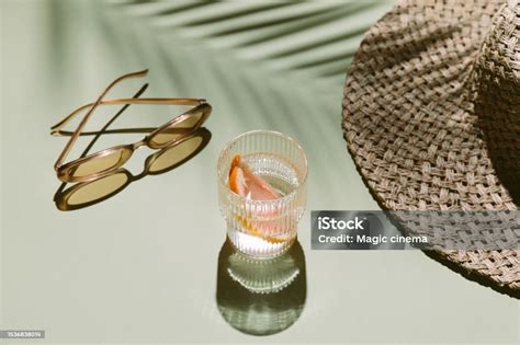 여름 플랫에는 밀짚 모자 선글라스 및 자몽 조각이있는 물 한 잔이 야자수 잎 그림자 태양 및 햇빛이있는 녹색 배경에 놓여 있습니다 휴가 휴일 여름 창조적 인 최소 개념