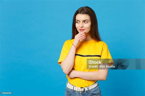 생생한 평상복에 웃는 잠겨있는 젊은 여자의 초상화 옆을 보고 스튜디오에서 밝은 파란색 벽 배경에 고립 된 턱에 손을 소품을 넣어 사람들 라이프 스타일 개념입니다 복사 공간을