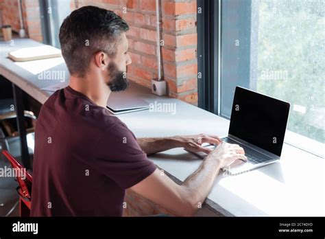 Selective Focus Of Bearded Businessman Using Laptop With Blank Screen In Modern Office Stock