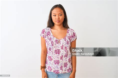 얼굴에 심각한 표정으로 고립 된 흰색 배경 위에 서있는 캐주얼 한 꽃 무늬 티셔츠를 입은 젊은 중국 여성 카메라를 보는 간단하고 자연스러운 T 셔츠에 대한 스톡 사진 및