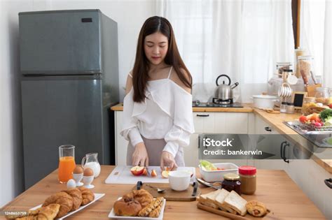 미소 짓는 젊은 아시아 여성은 부엌에 서서 샐러드를 위해 건강한 빵 채소와 과일을 준비합니다 건강 다이어트 글루텐 프리 컨셉 을 관리하십시오 가정 생활에 대한 스톡 사진 및