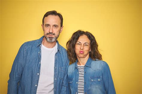 아름 다운 중년 부부는 함께 재미 있는 얼굴과 고립 된 노란색 배경 퍼핑 뺨 위에 데님 셔츠를 입고 공기 미친 표정으로 입이