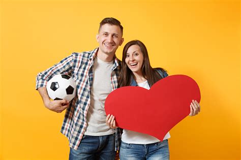 젊은 행복 한 명랑 커플 팬 여자 사람 축구 팬 들 응원 지원 팀 레드 심장 사랑 노란 배경에 고립 된 축구공을 들고 스포츠 가족 레저 사람들 라이프 스타일 개념