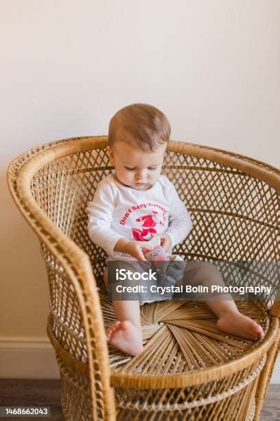 맨발로 등나무 의자에 앉아 티더를 가지고 노는 귀여운 13개월 된 남자 아기 흰색 긴팔 바디수트 아래에 천 기저귀를 차고 Dont Stop Believing이라는 단어가