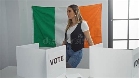 Young Attractive Blonde Woman Voting In An Irish Electoral College Room With Irish Flag In The