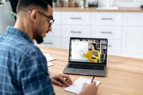 원격 온라인 수업 여자 선생님과 함께 노트북 화면에서 한 남자 학생의 어깨 너머로보십시오 그 사람은 원격으로 공부하고 강의를 듣고 노트북에서 메모를하고 지식을 습득합니다