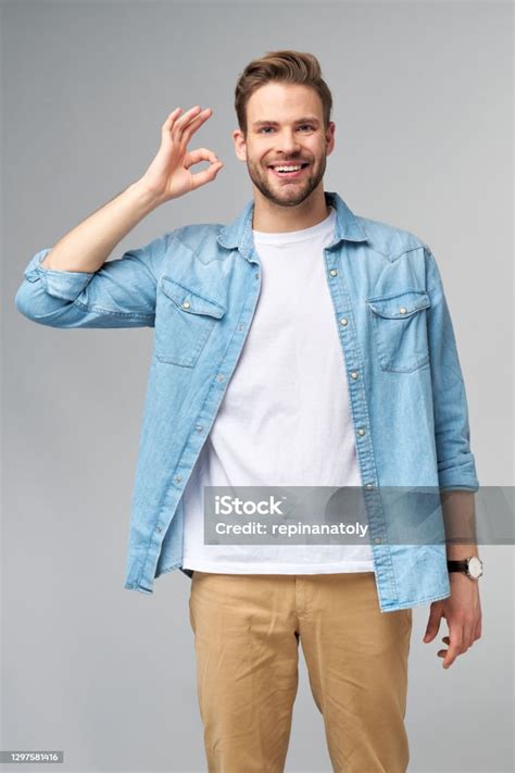 청바지 셔츠를 입은 젊은 잘생긴 백인 남자의 초상화가 밝은 배경 위에 서 있는 확인 사인 제스처를 보여줍니다 25 29세에 대한 스톡 사진 및 기타 이미지 Istock