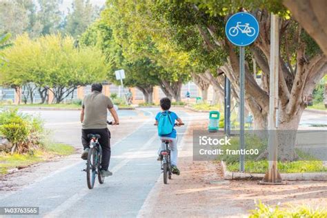 자전거 타는 사람 아빠와 아들은 페인트 포장 도로와 도로 표지판이있는 공원에서 자전거 길을 따라 타고갑니다 도시의 환경 친화적 인 교통 인프라와 안전 자전거 타기에 대한