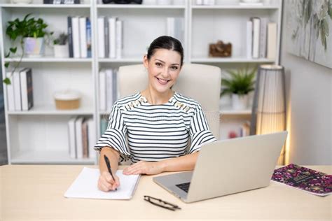 Brunette Adult Female Model Working At Computer In Office Wearing Striped Dress Stock Photo