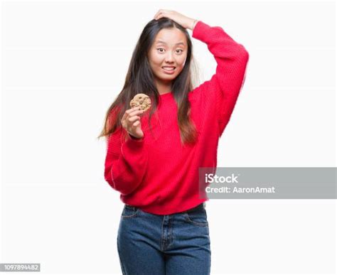 젊은 아시아 여자 머리에 손으로 압박 고립 된 배경 위에 초콜릿 칩 쿠키를 먹는 충격 수치심과 깜짝 얼굴로 분노와 좌절 두려워