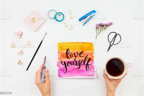 Flatlay 손 글자 동기와 사랑 자신 수채화 브러쉬 여자의 손을 잡고 차 한잔 및 기타 고정 용품 서명 레터링 연습 교육 또는 창의력의 개념 가위에 대한 스톡 사진 및