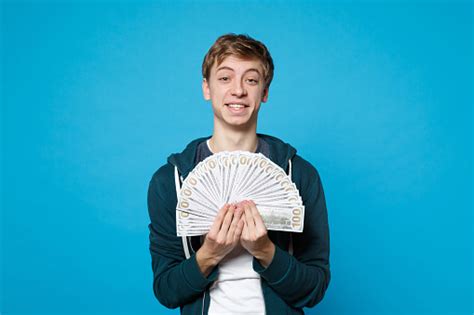 달러 지폐에 돈의 팬을 들고 캐주얼 옷에 예쁜 젊은 남자를 웃는 현금 돈은 스튜디오에서 파란색 배경에 고립 사람들은 진심으로 감정 라이프 스타일 개념입니다 복사 공간을 모의