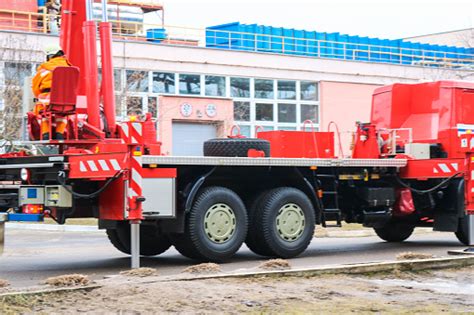 소방복을 입은 소방관 구조대는 소방차에서 화재를 진압하고 파이프와 장비가 있는 대형 산업 공장에서 사다리 요람 리프트를 꺼내기 위해 왔습니다 0명에 대한 스톡 사진 및 기타